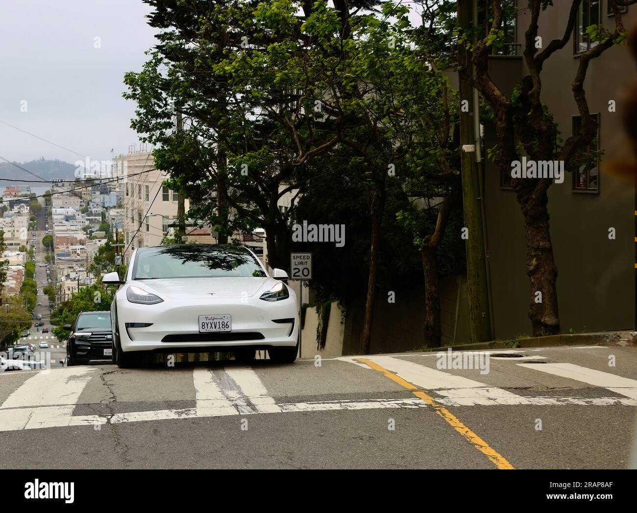 View downhill of typical street with a white Tesla Model 3 reaching the ...