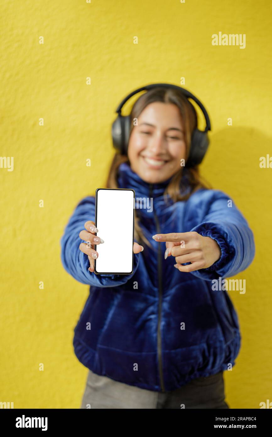 Latin girl with headphones out of focus shows the blank screen of her ...