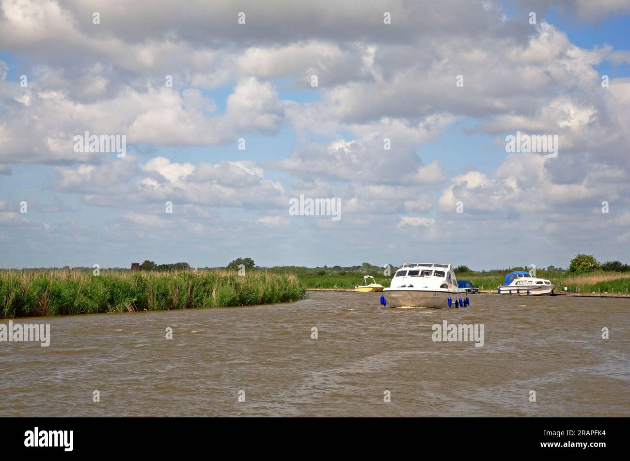 A view of a cruiser making way on the River Bure downstream of Acle on ...