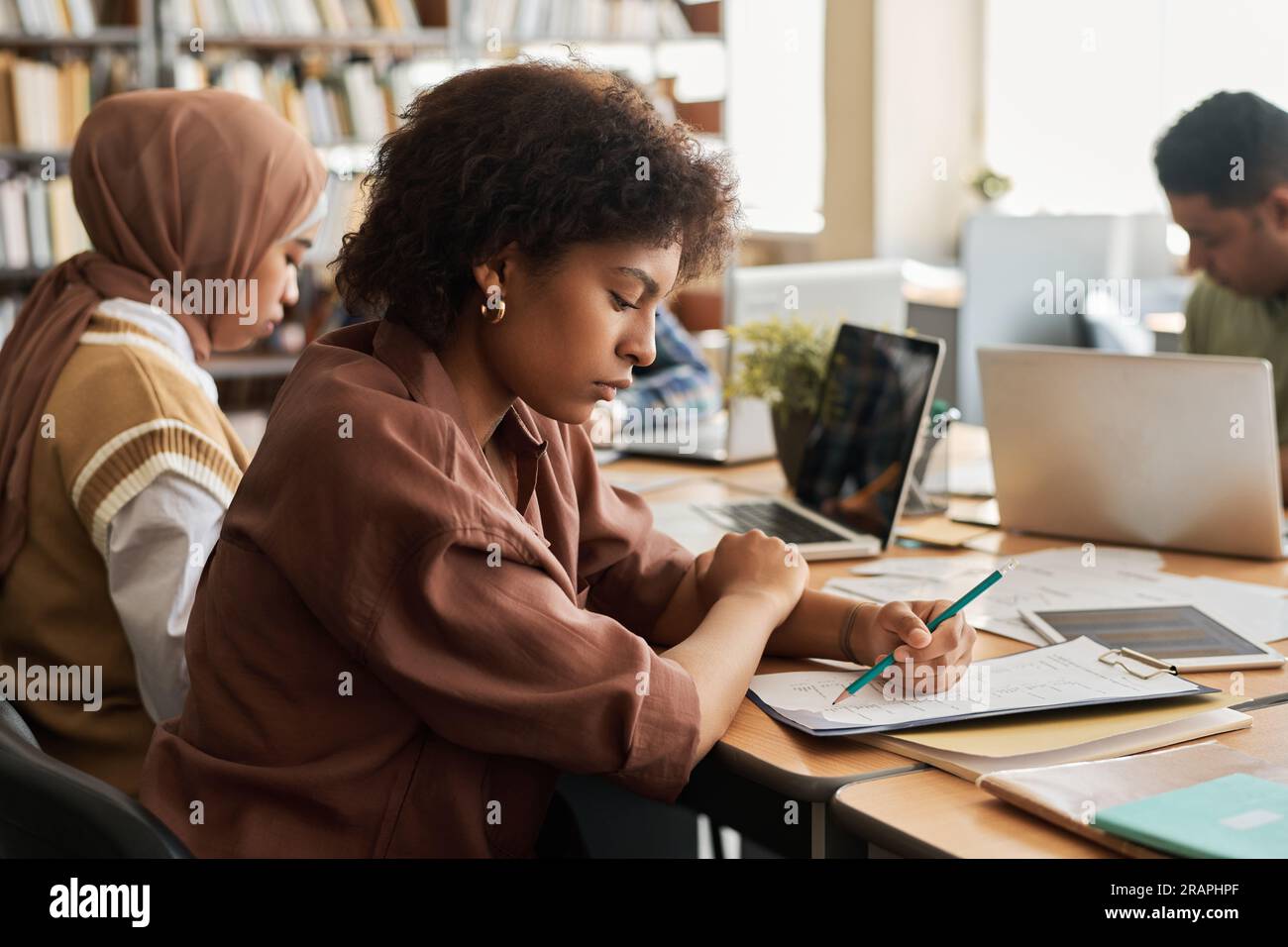 African American girl writing foreign language test at table with other ...