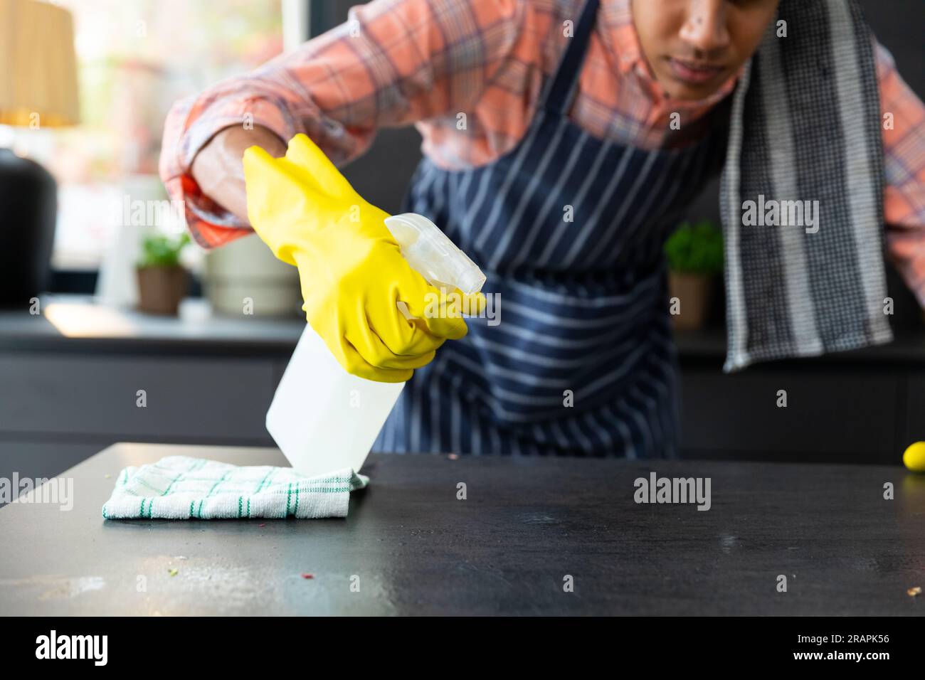 Midsection of biracial man wearing apron and rubber gloves cleaning ...