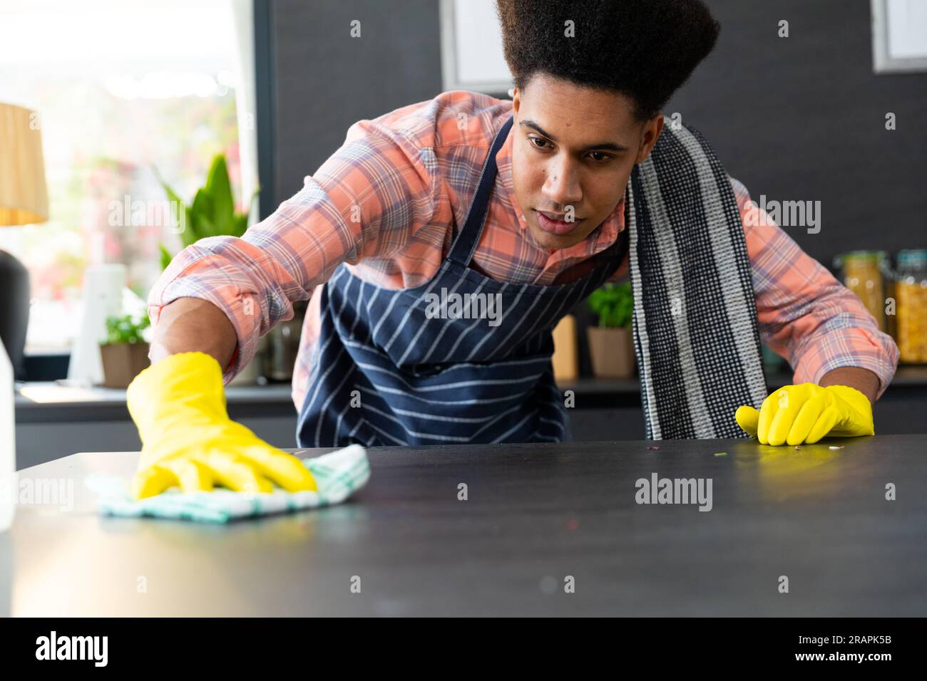 Focused biracial man wearing apron and rubber gloves cleaning ...