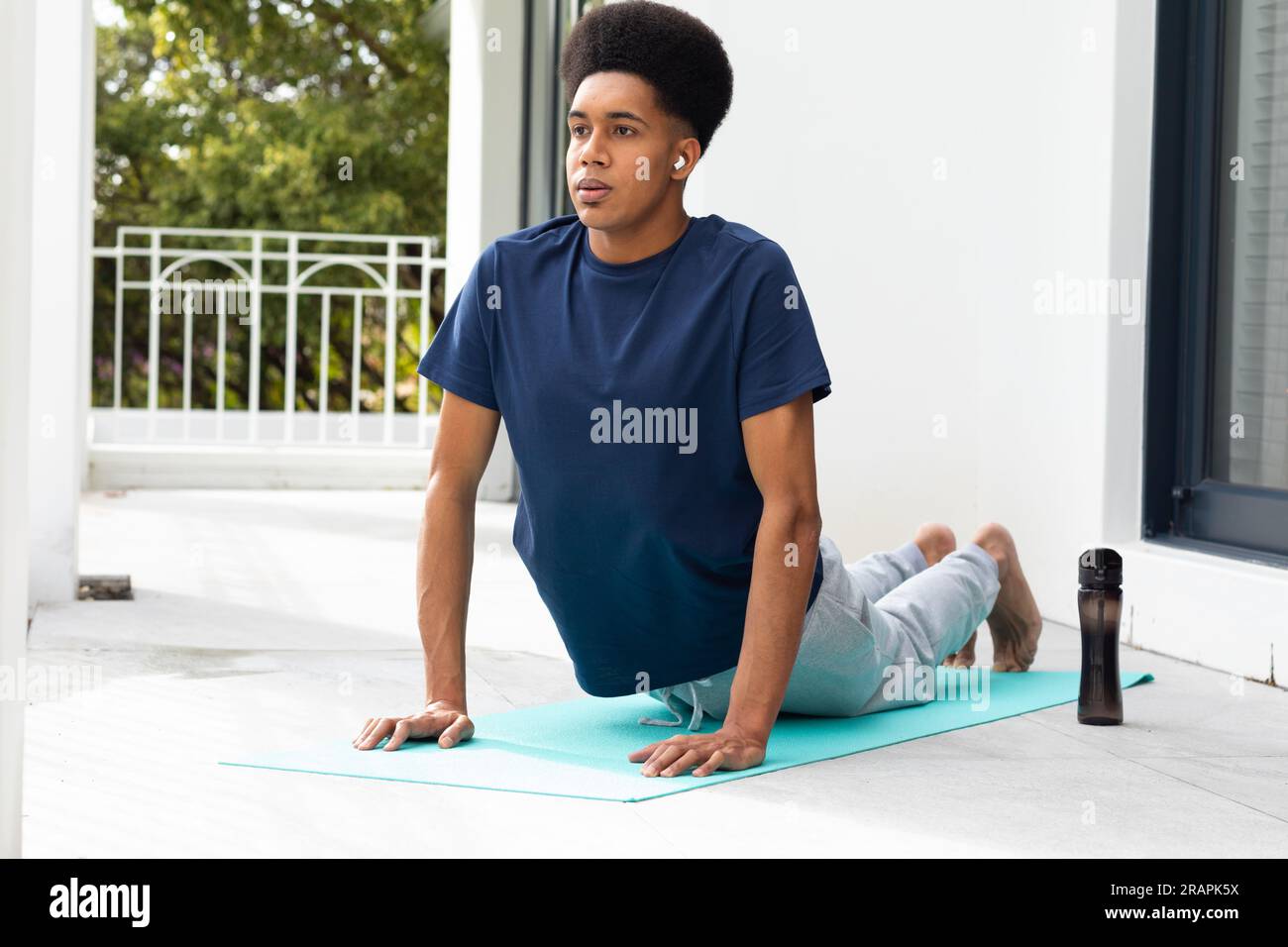 Focused biracial man doing yoga lying on sunny balcony. Cobra pose ...