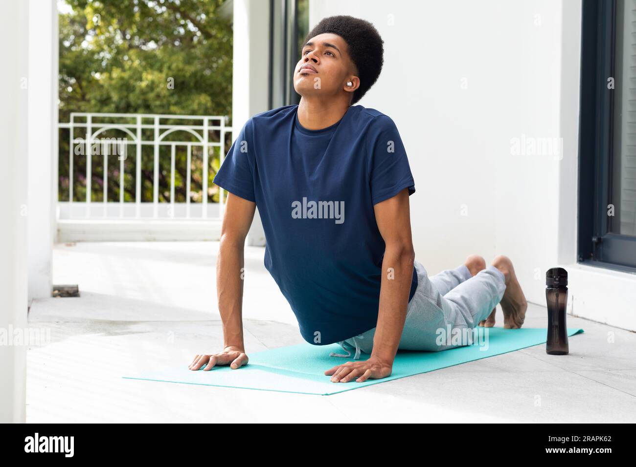 Focused biracial man doing yoga lying on sunny balcony. Cobra pose ...