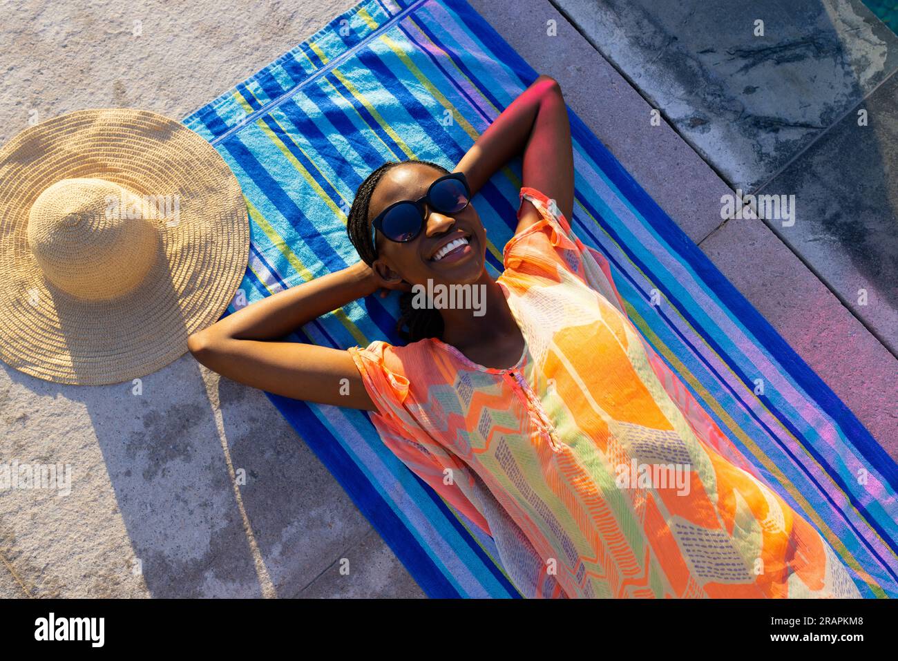 Portrait of african american woman lying on towel and sunbathing next ...