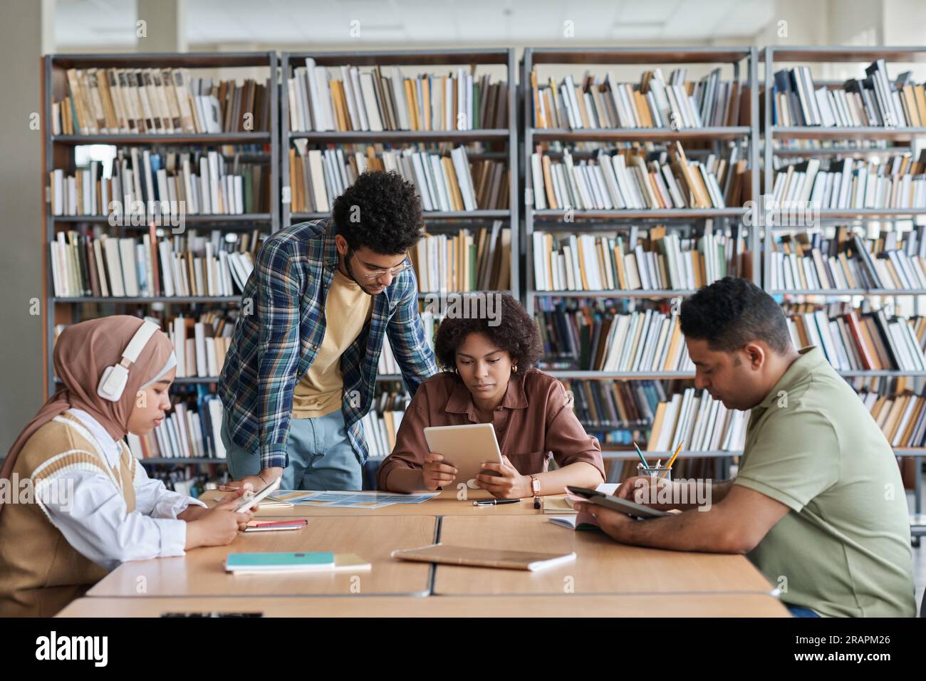 Group of students studying together in the library, they using gadgets ...