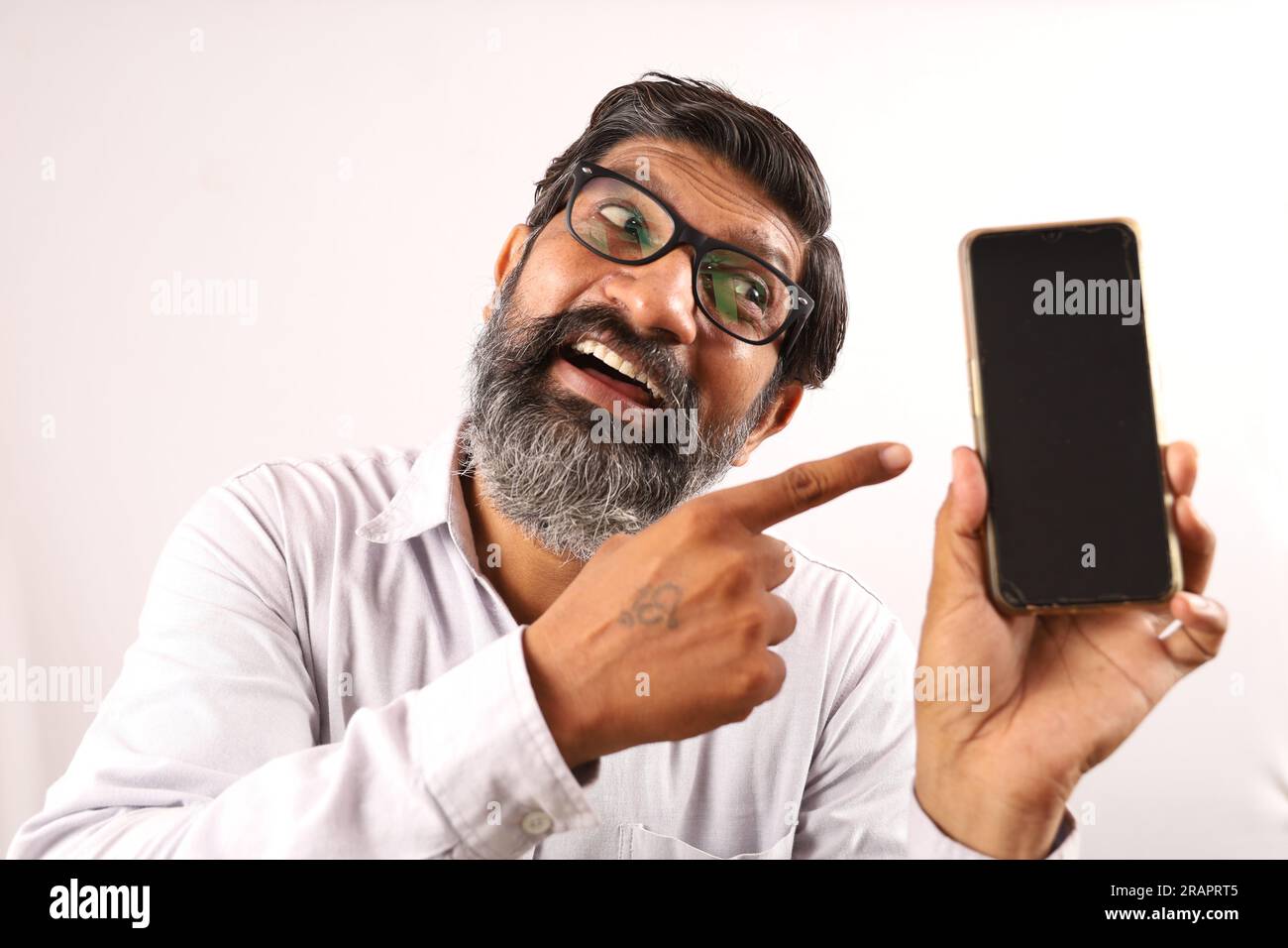 mid aged Indian bearded man wearing shirt holding and showing a mobile phone in his hand. Funky ...