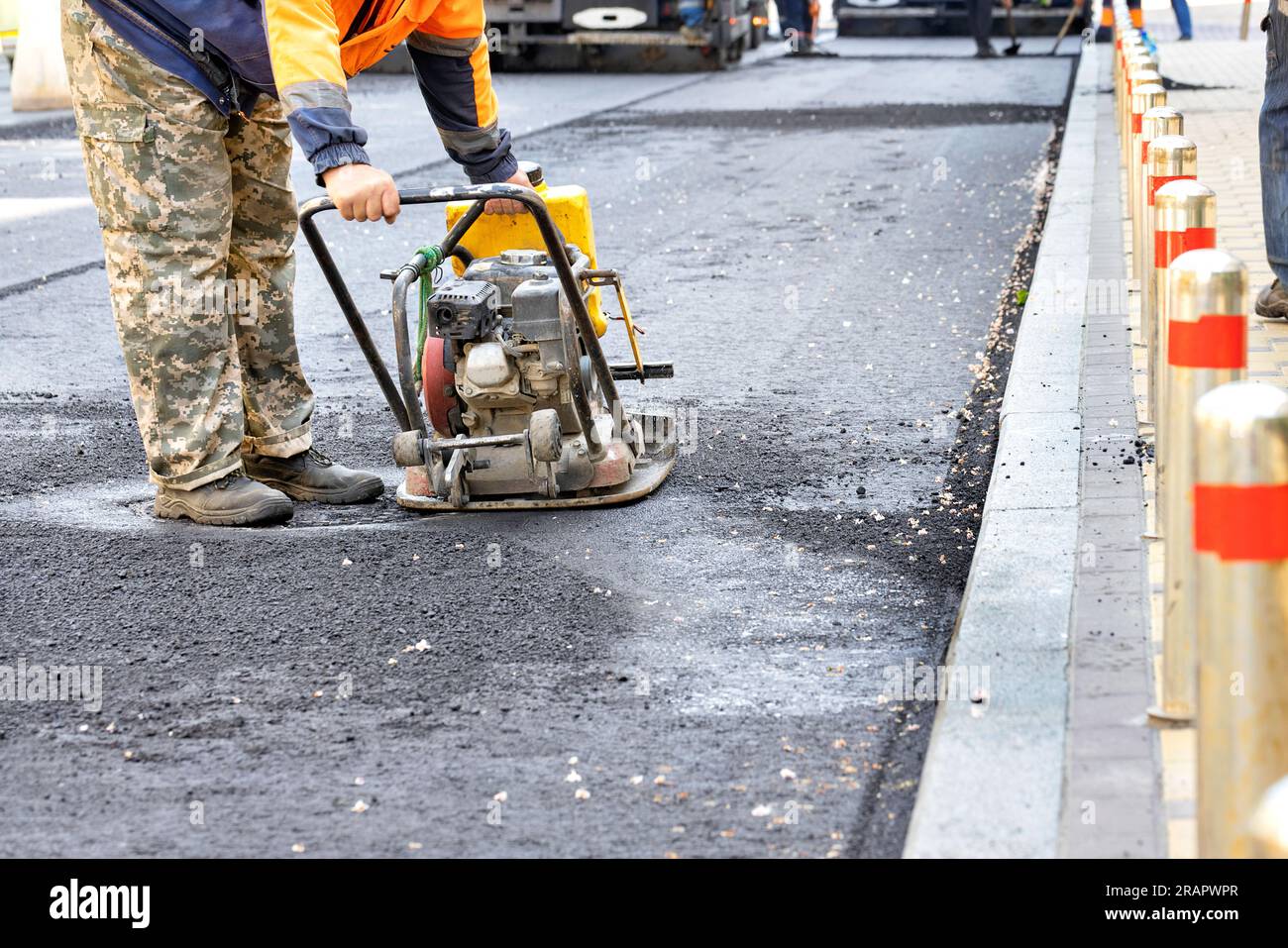 A road service worker ramming fresh asphalt on a stretch of road with ...