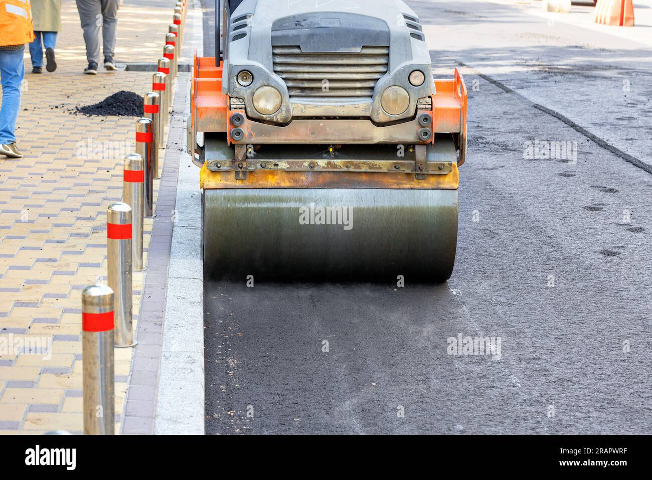 A vibrating roller compacts fresh asphalt on a city street on a sunny ...