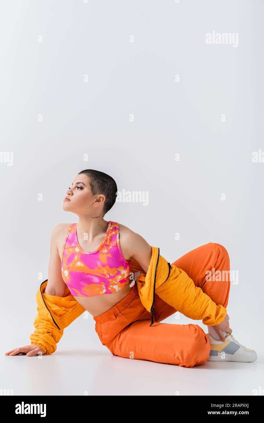vibrant youth, tattooed young woman with short hair sitting on grey ...