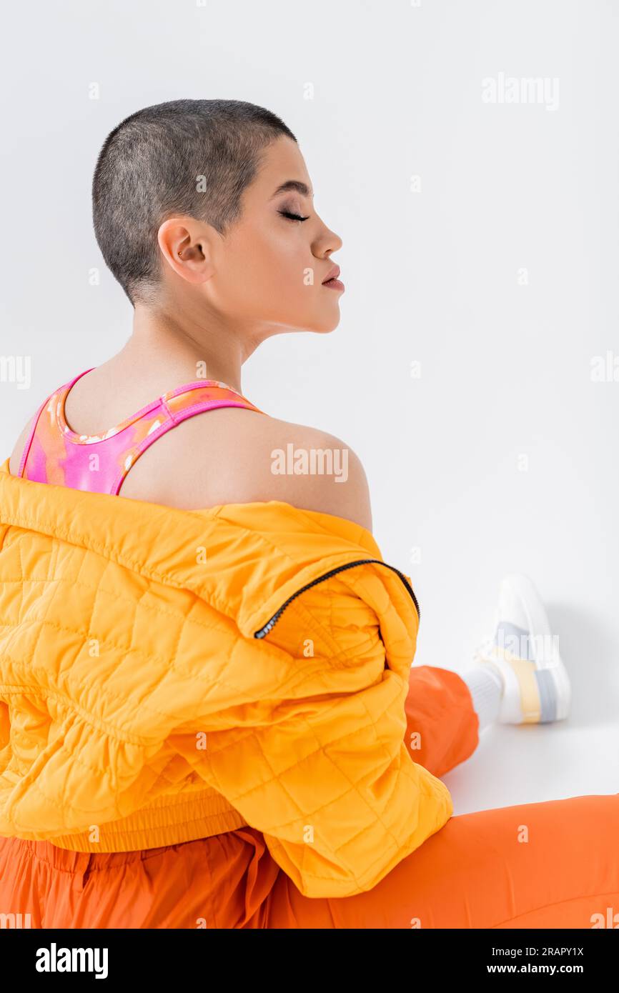 urban fashion, young woman in colorful clothes posing on grey ...