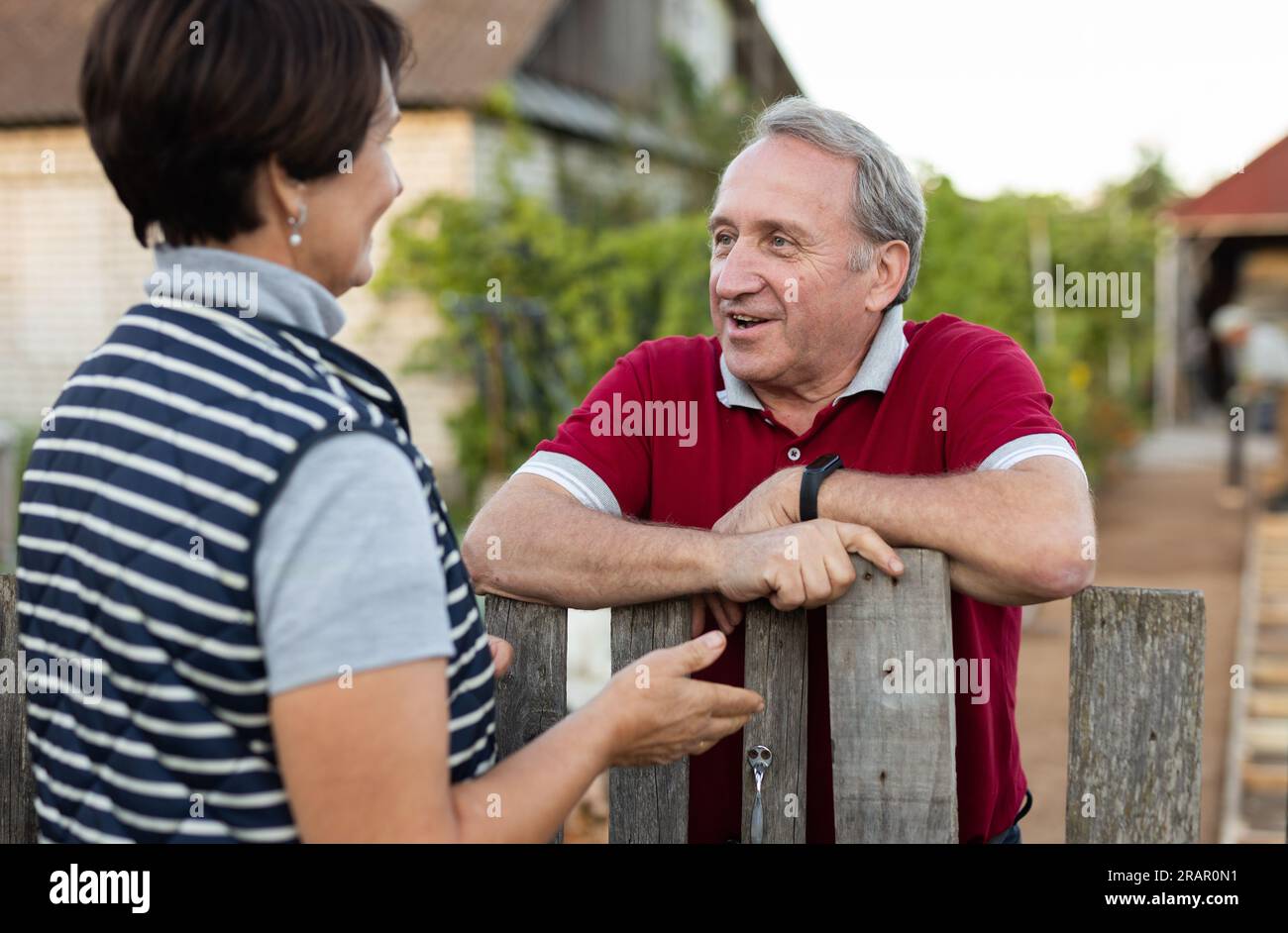 Two gardeners friendly talking outdoors next to wooden fence of country ...