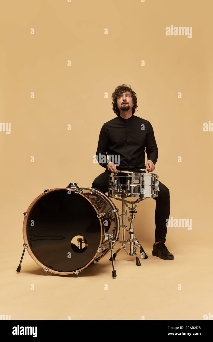 Stylish man, talented musician playing drums against light brown studio ...