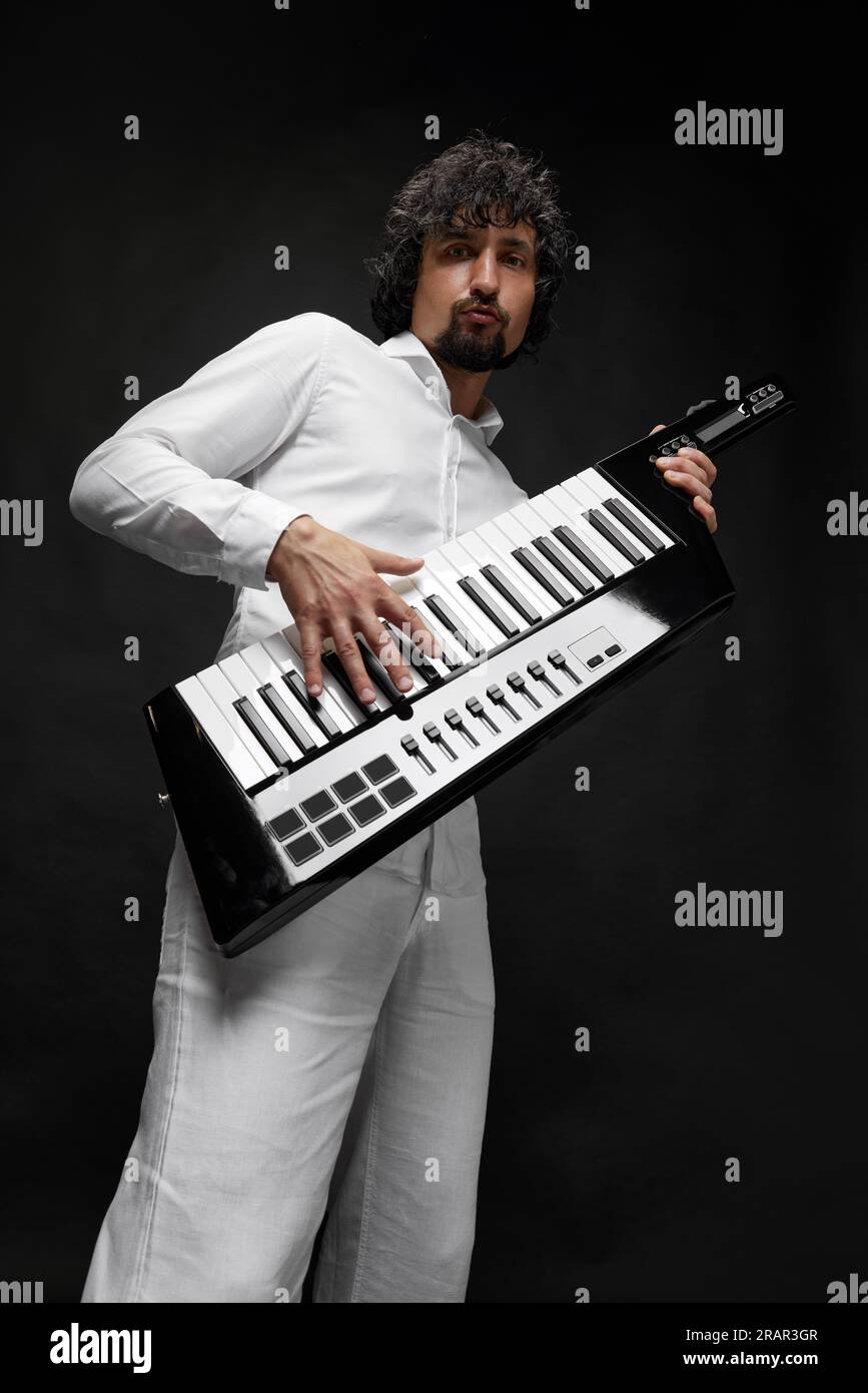 Portrait of stylish bearded man in white suit playing synthesizer ...