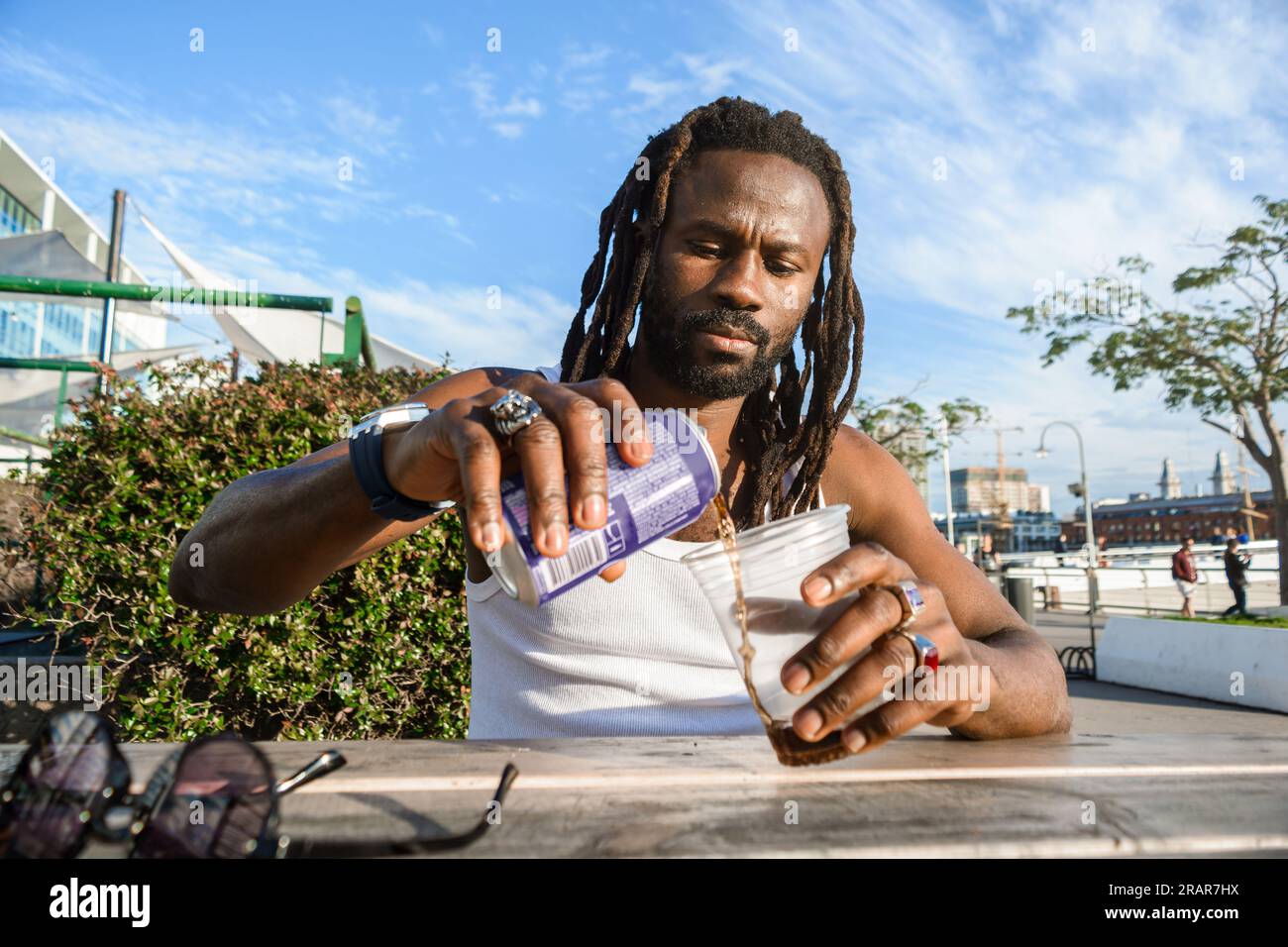 front view of young black man with dreadlocks, sitting outdoors at ...