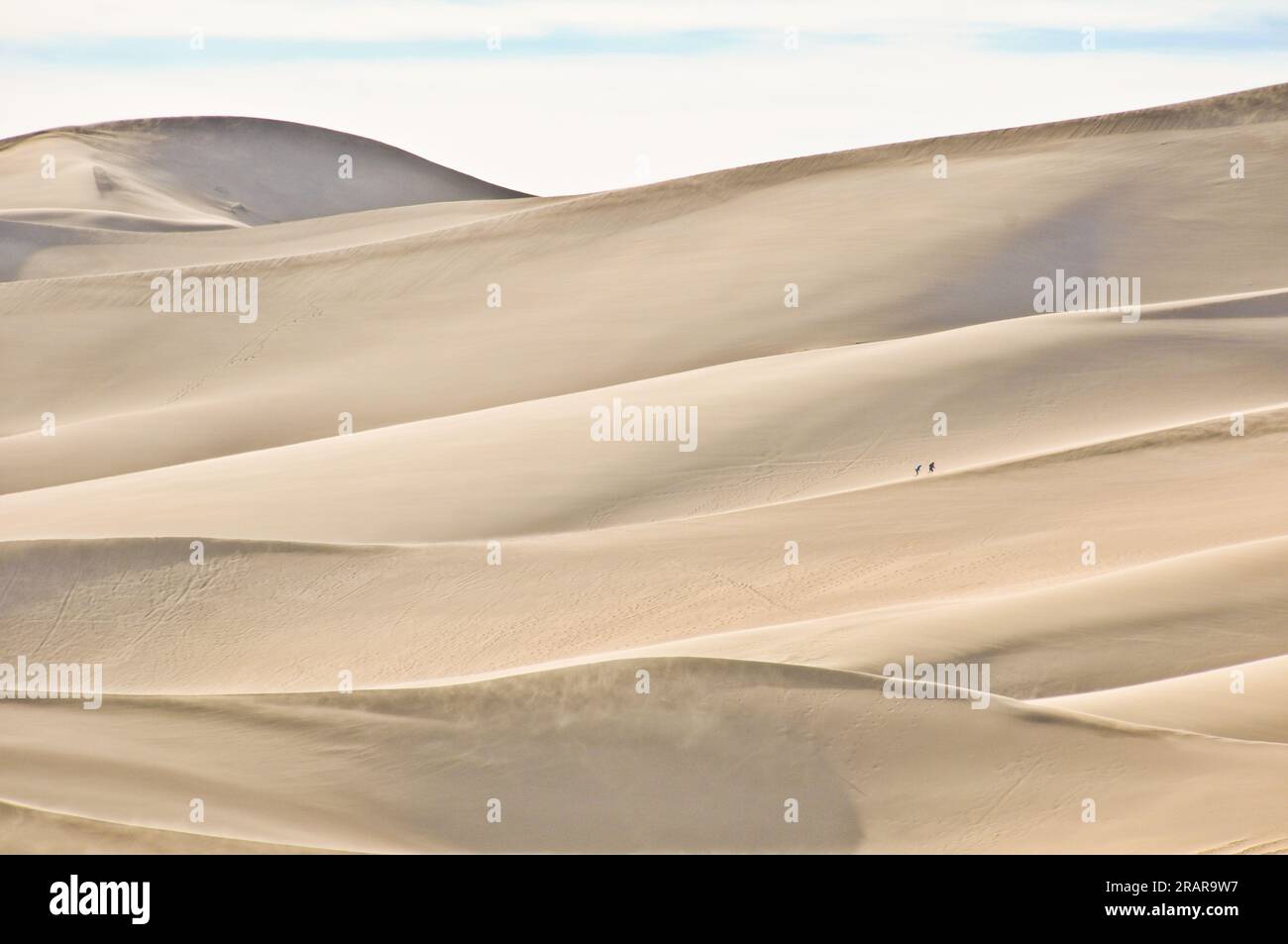 Two hikers climbing an enormous sand dune in the desert at Great Sand ...