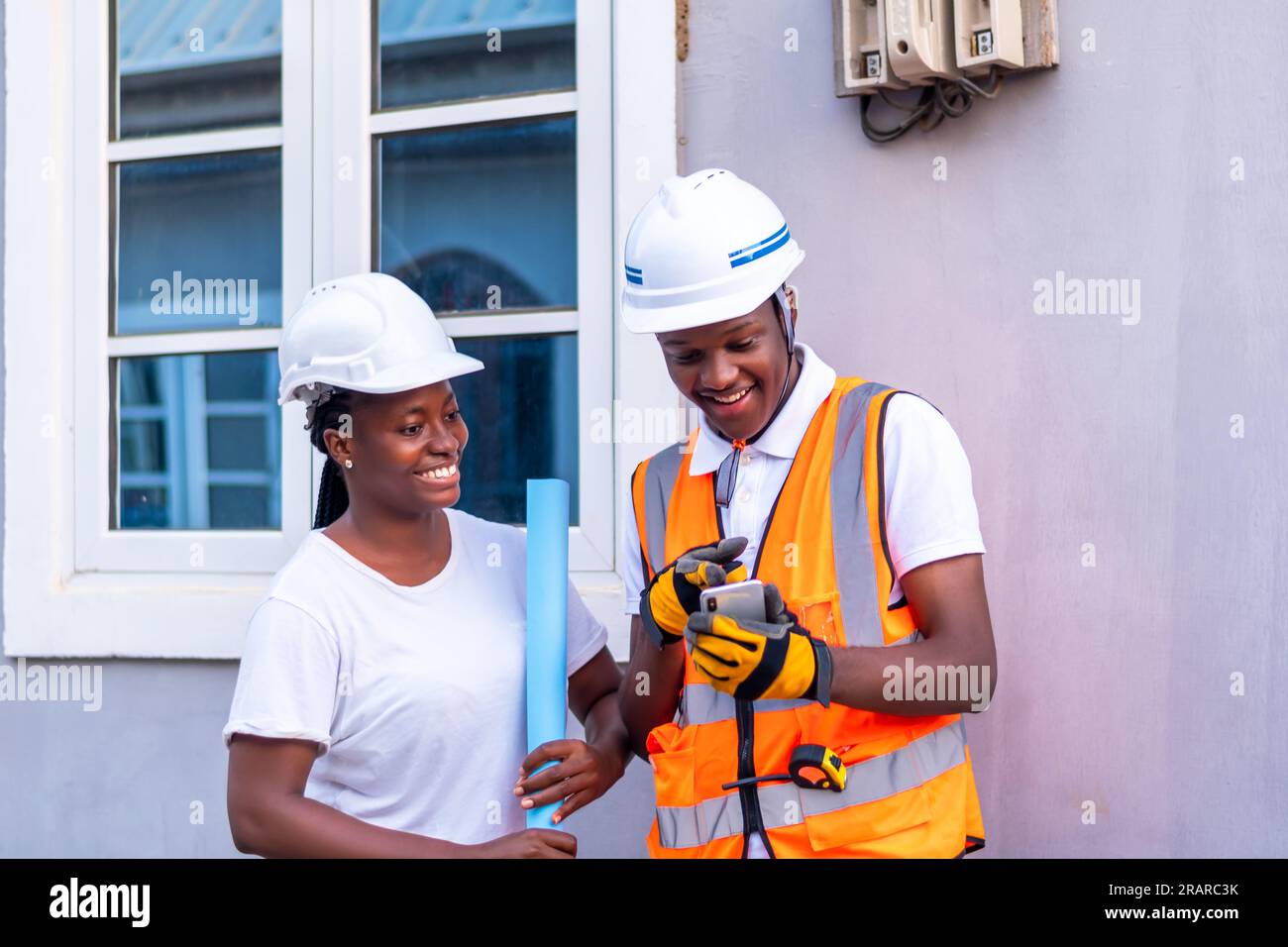 Two industrial contractors using mobile phone, standing and smiling ...