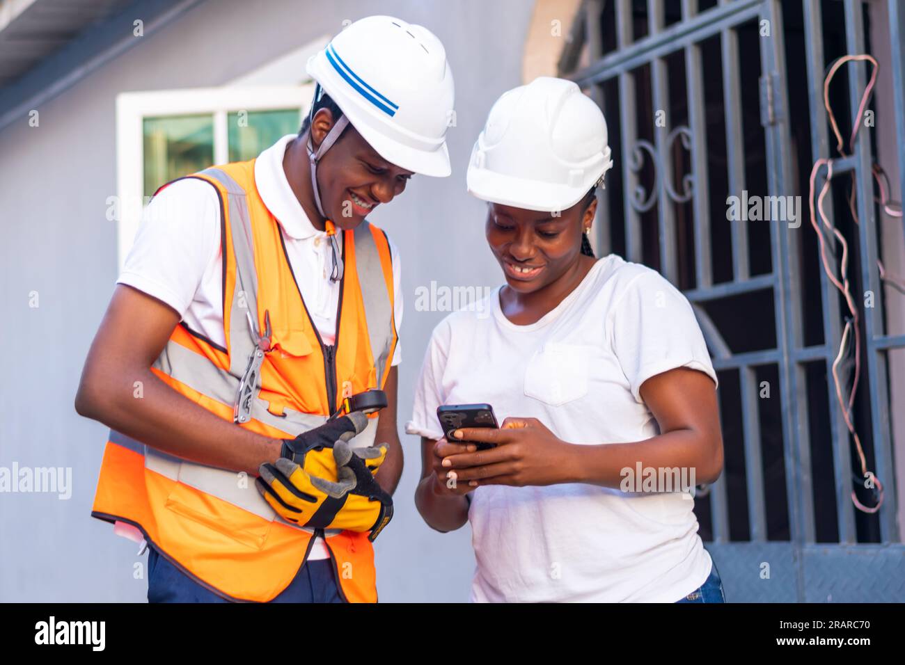 Two industrial contractors using mobile phone, standing and smiling ...