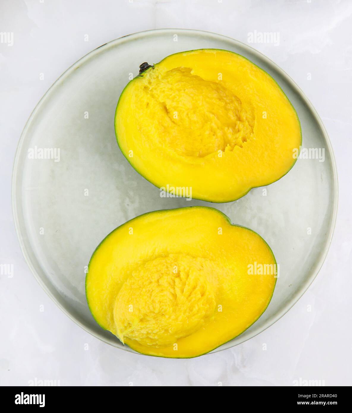 Ripe mango fruit sliced into halves on a plate isolated on grey marble ...