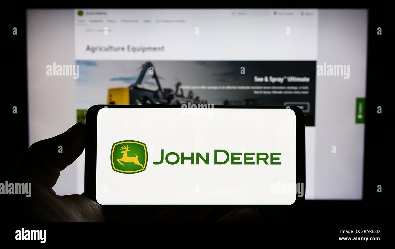 Person holding mobile phone with logo of American business Deere and ...