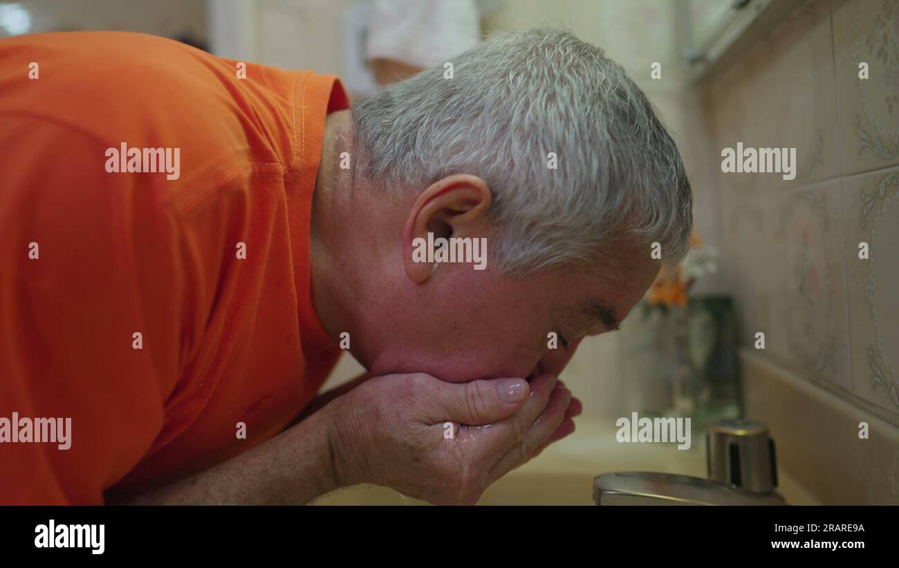 Older man washing face by bathroom sink during morning routine ...