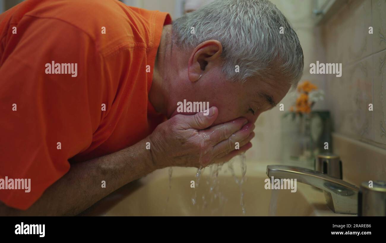 Older man washing face by bathroom sink during morning routine ...