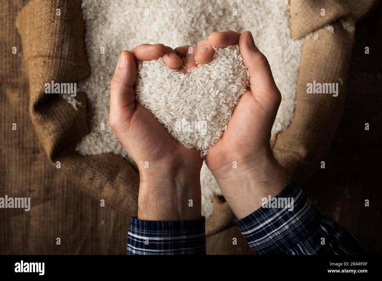 Human hands in shape of heart holding handful of rice over burlap sack ...