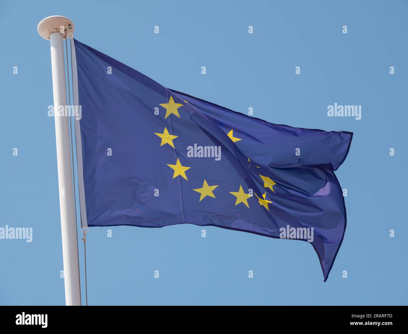European Union (EU) flag waving in the wind on a flagpole with blue sky ...