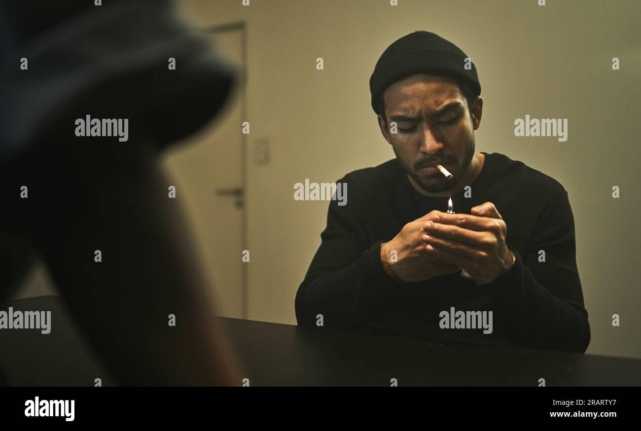 Man, smoking and talking to police detective in interrogation room with ...