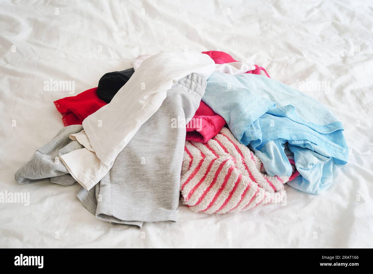 Messy colorful clothing on white bed background at home Stock Photo - Alamy