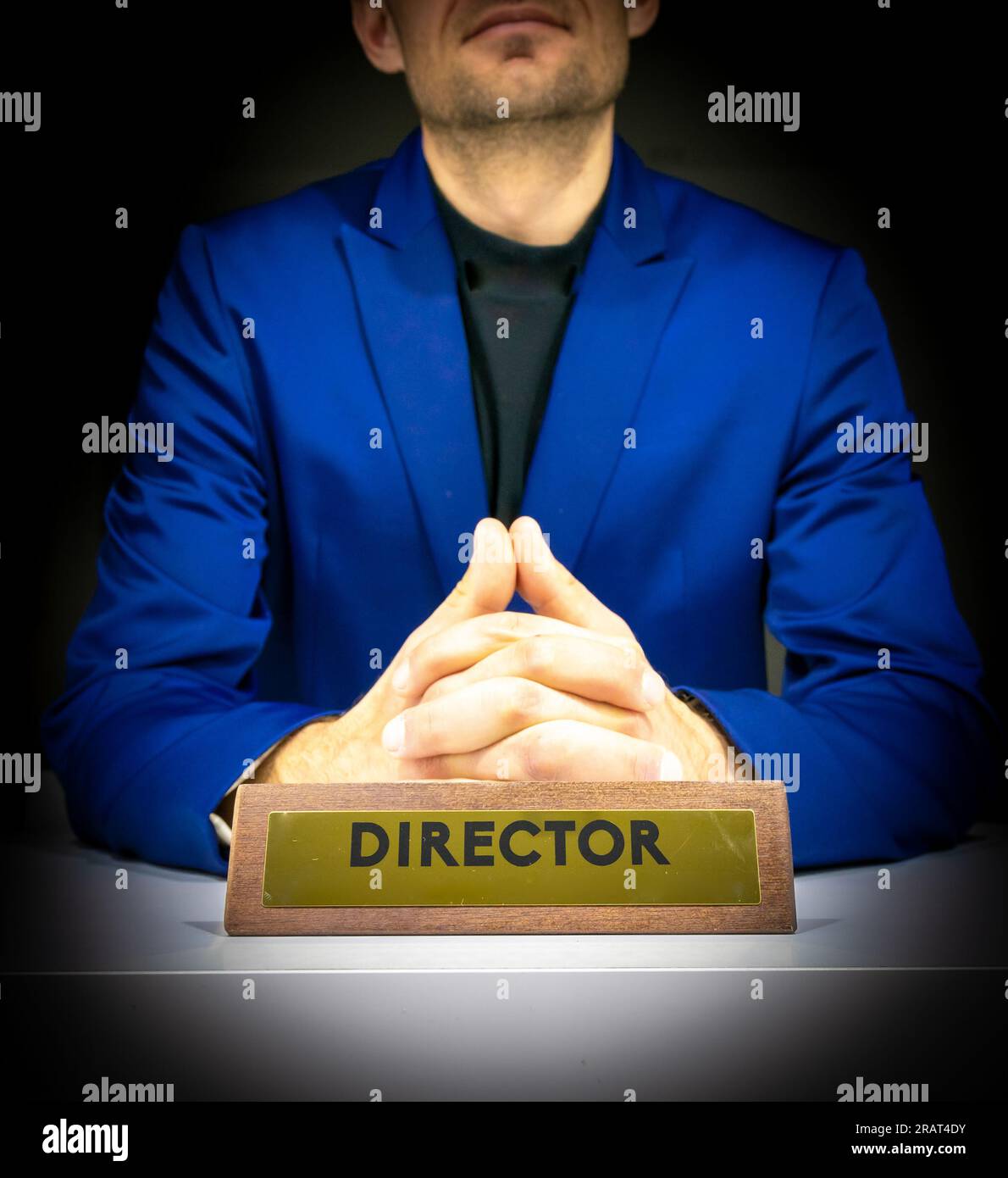 Person in blue suit sits dark room with office position plate "Director ...