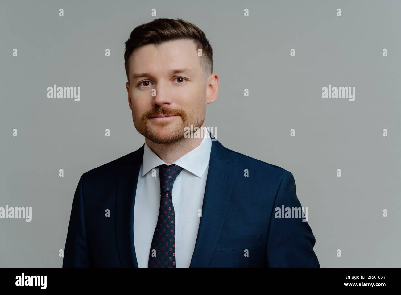Young successful bearded businessman in suit, confident CEO, headshot posing, grey studio ...