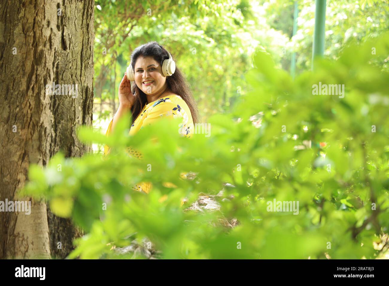 A mid aged obese woman listening and enjoying to music in a park using ...