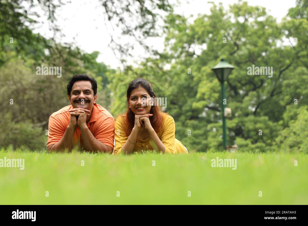 Young happy couple leaning together on grass in a public park early ...