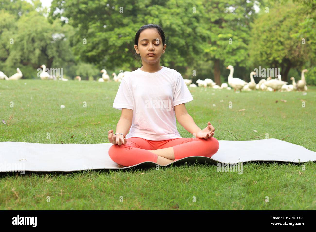 Young kid doing yoga exercises early morning in a green public park. We ...