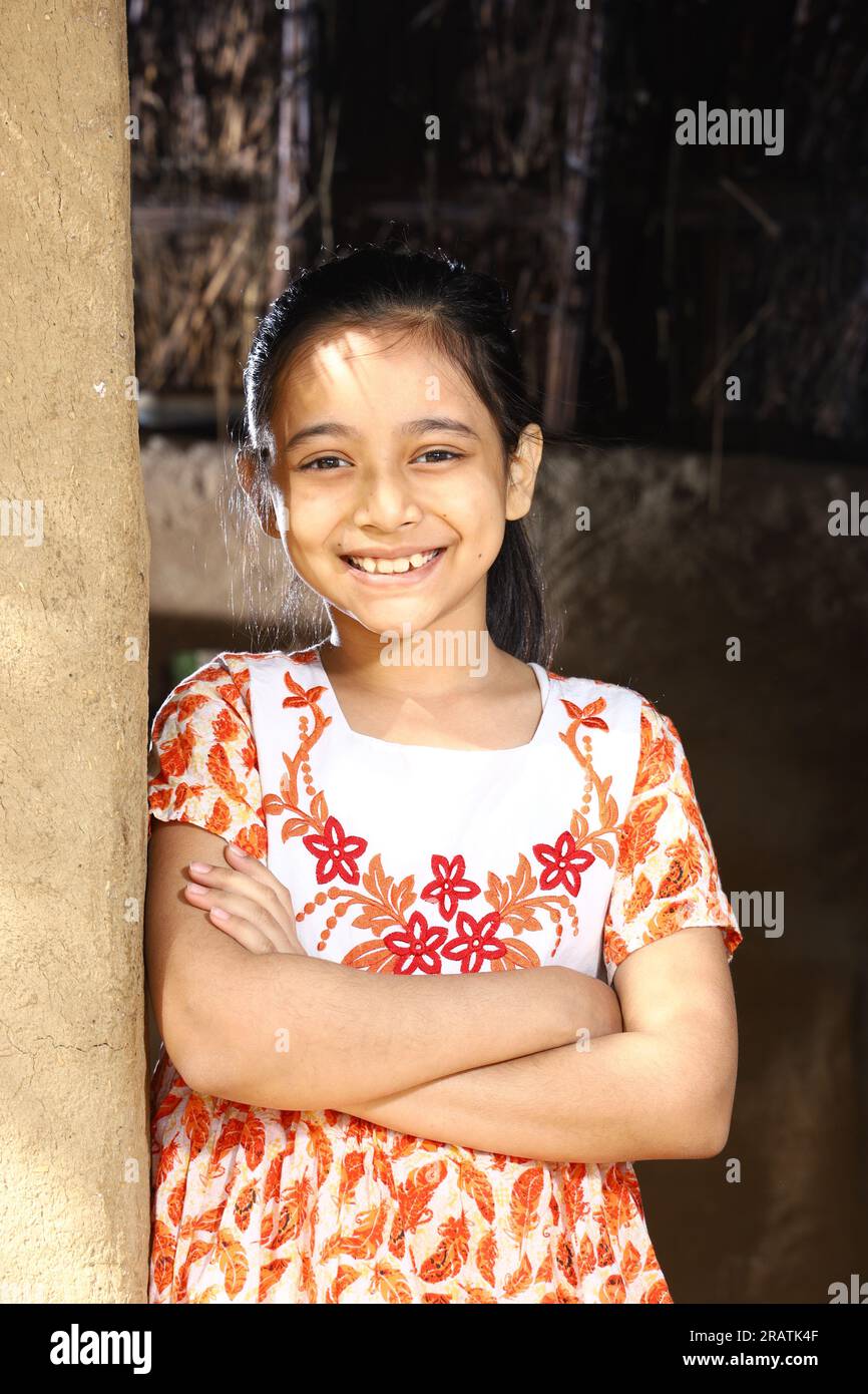Happy rural Indian girl standing on her cottage gate wearing a gown ...
