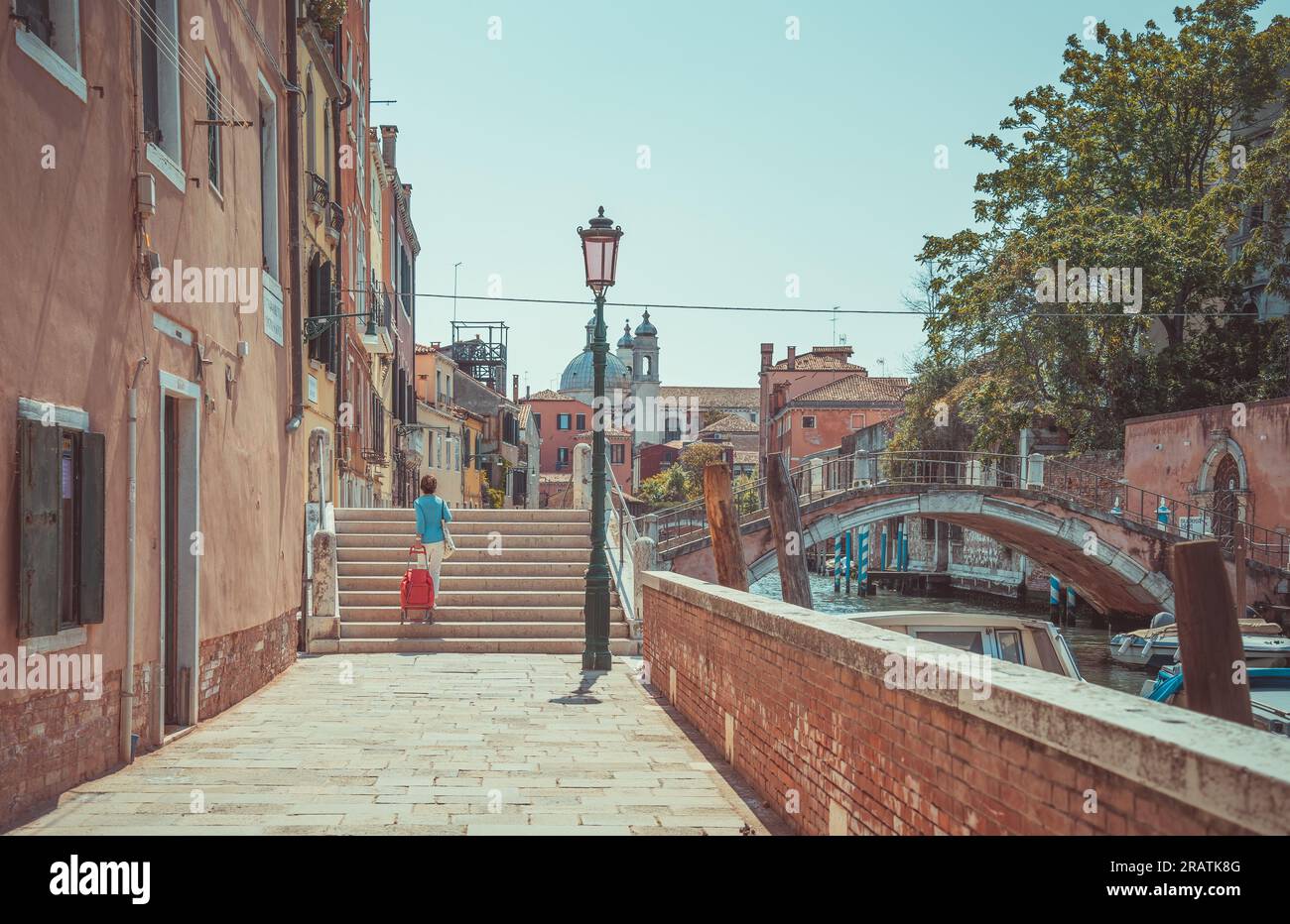 unidentifiable tourist woman with a luggage trolley crossing a bridge ...