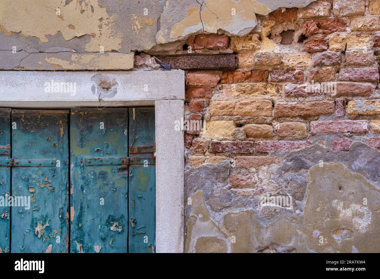 Detail with a green wooden shutter window on a worn out plastered red brick wall, in Venice ...