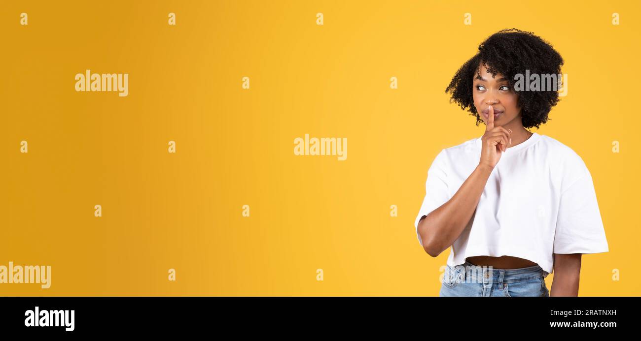 Positive serious young black woman in casual making shh gesture with ...