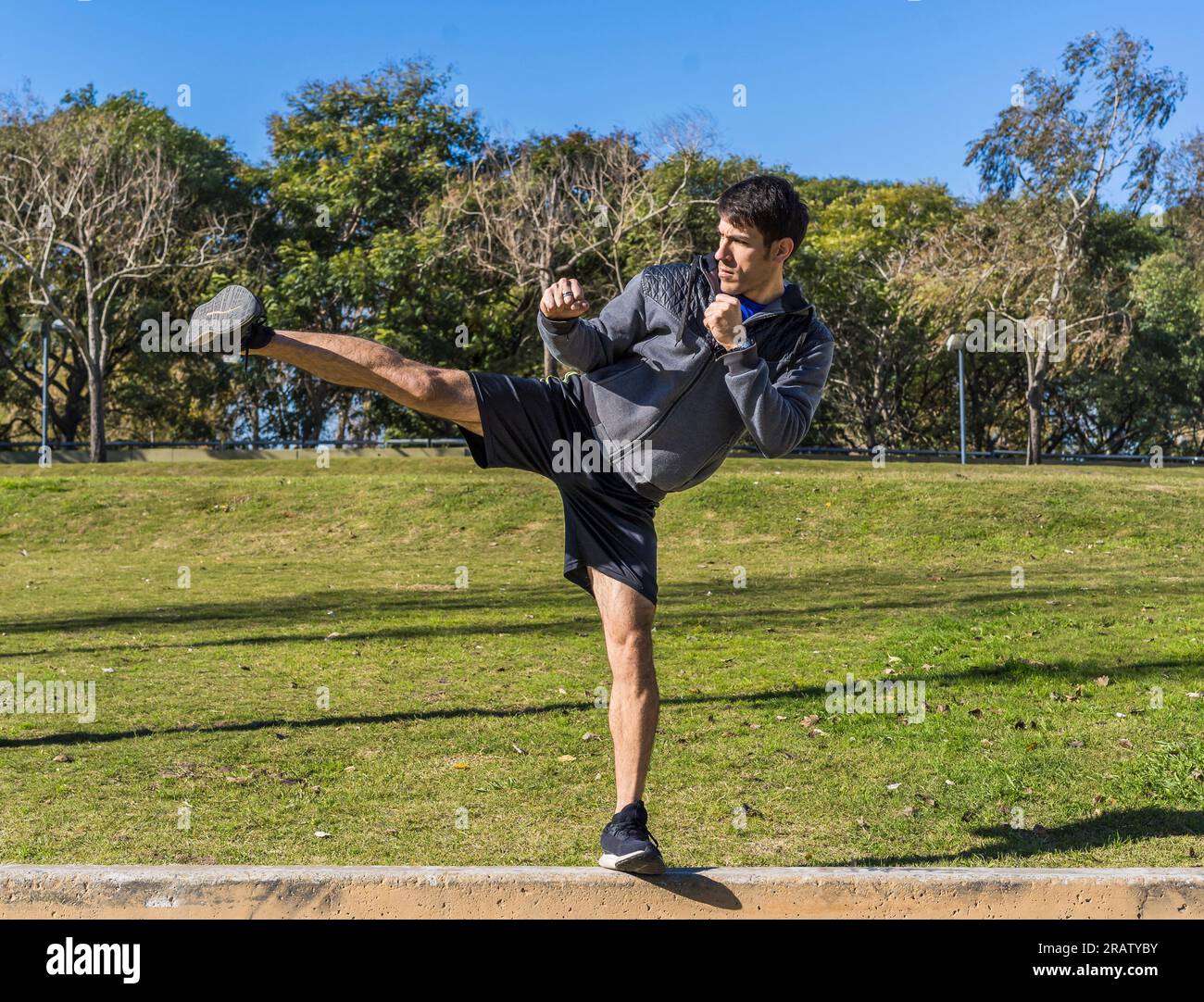 Young athletic martial arts fighter practicing kicks in a public park ...