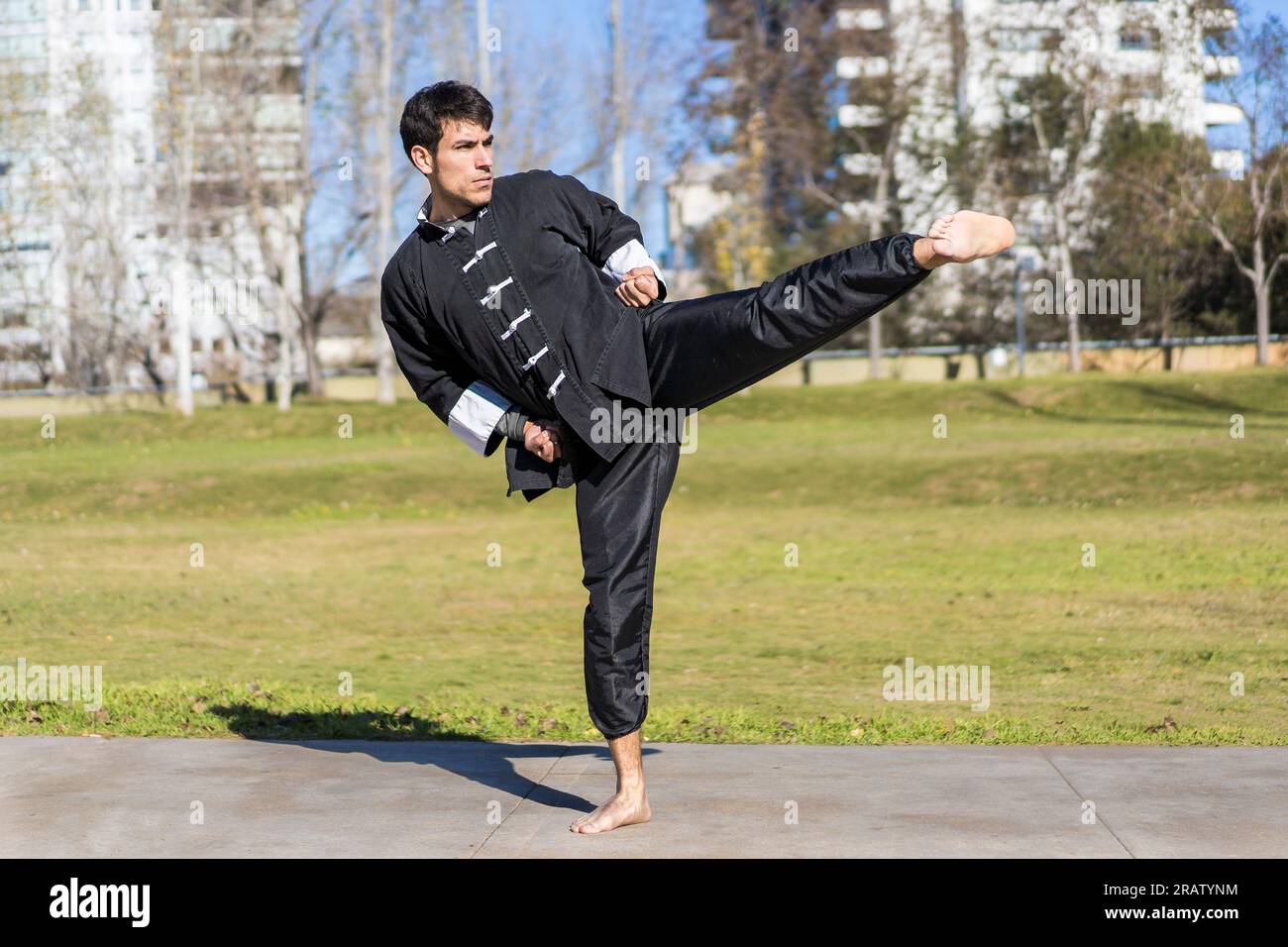 Young athletic martial arts fighter practicing kicks in a public park ...