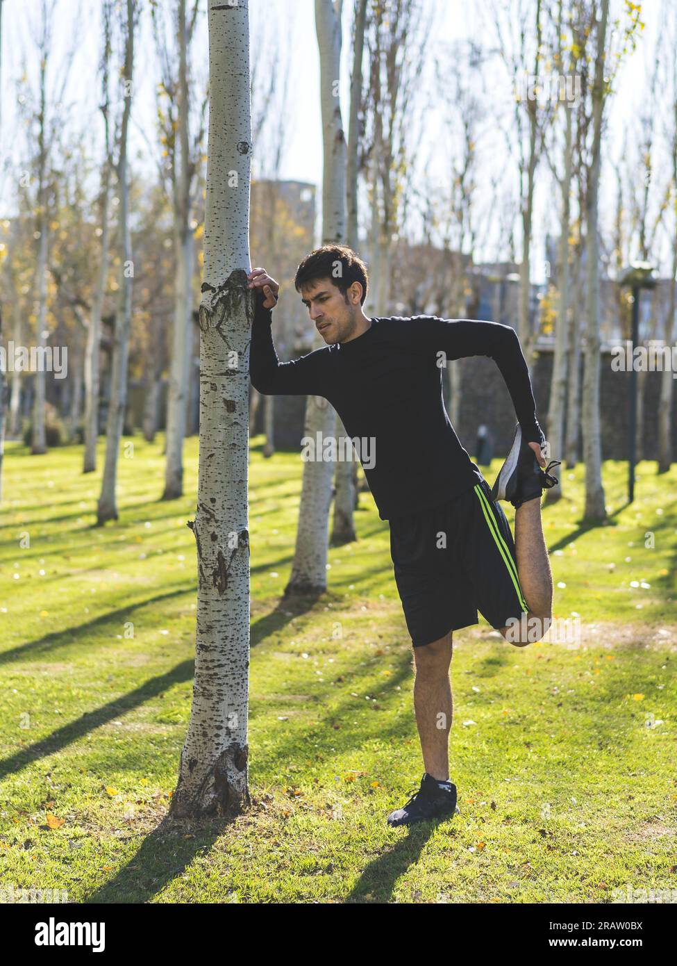 Attractive man leaning against a tree stretching his quadriceps Stock ...