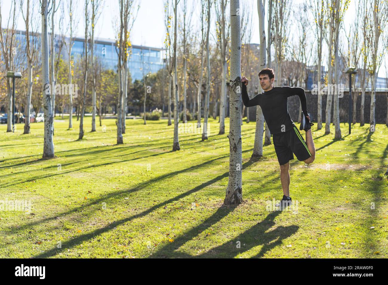 Attractive man leaning against a tree stretching his quadriceps. Copy ...