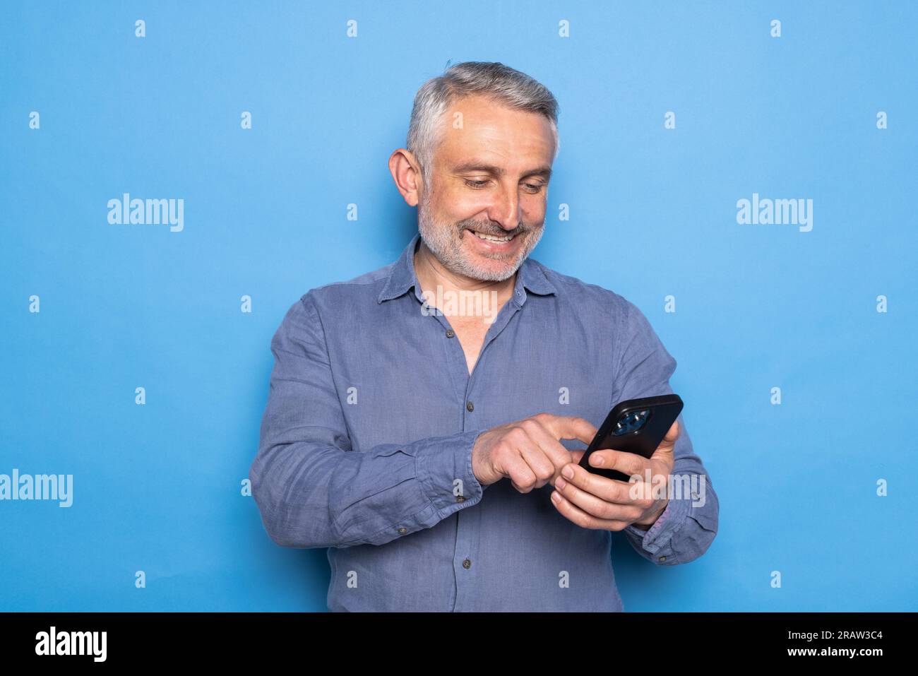 Happy relaxed man holding his mobile phone as he stands smiling at the ...
