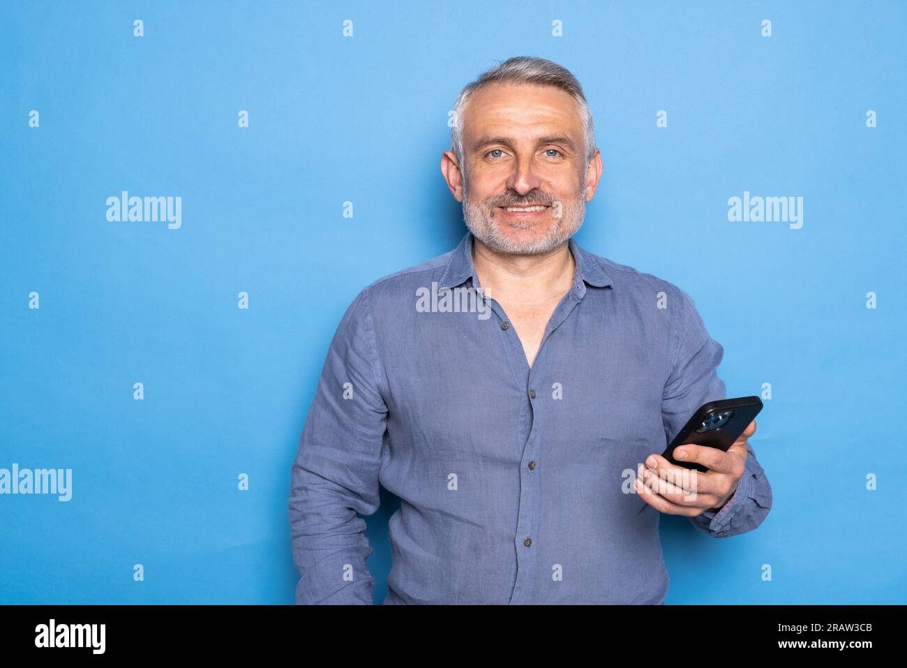 Happy relaxed man holding his mobile phone as he stands smiling at the ...