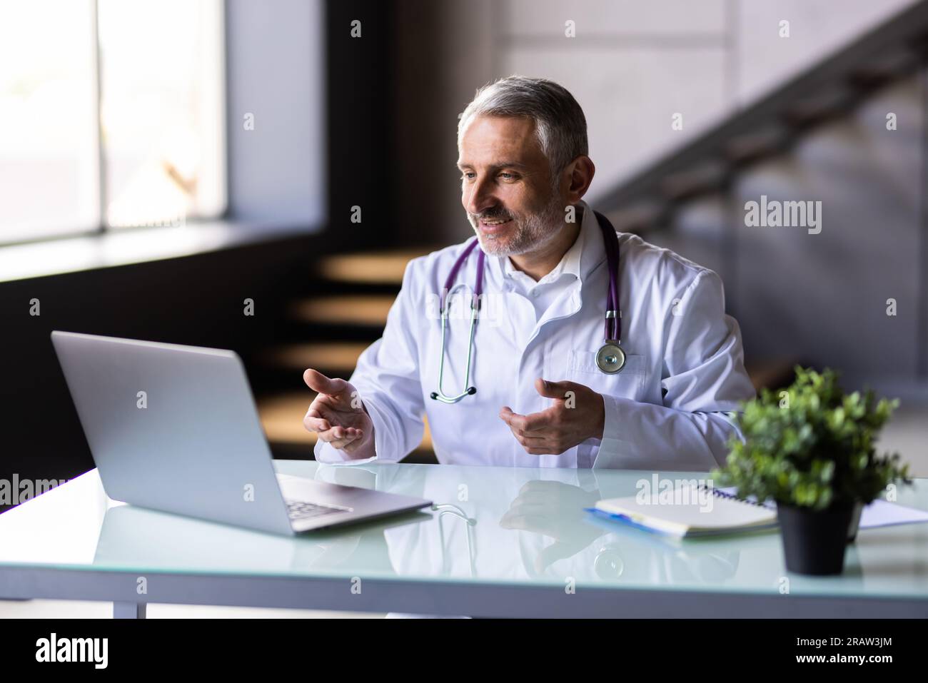 Doctor man sitting at the desk at his working place and smiling at ...