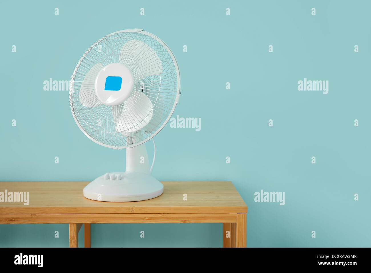 Wooden table with modern electric fan near blue wall Stock Photo - Alamy
