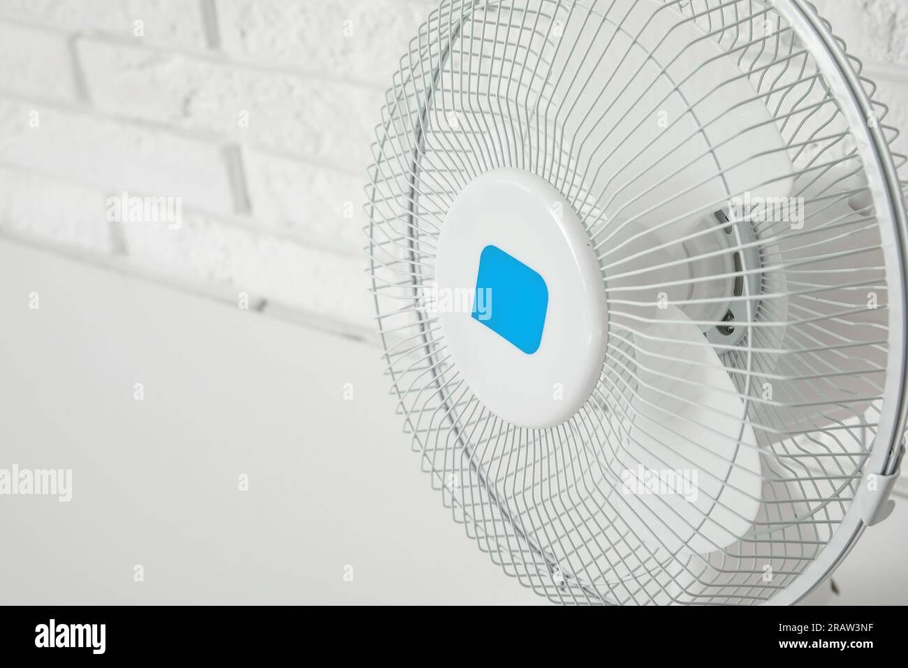 Table with modern electric fan near white brick wall Stock Photo - Alamy