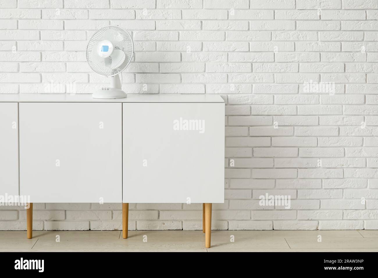 Stylish cabinet with modern electric fan near white brick wall Stock ...