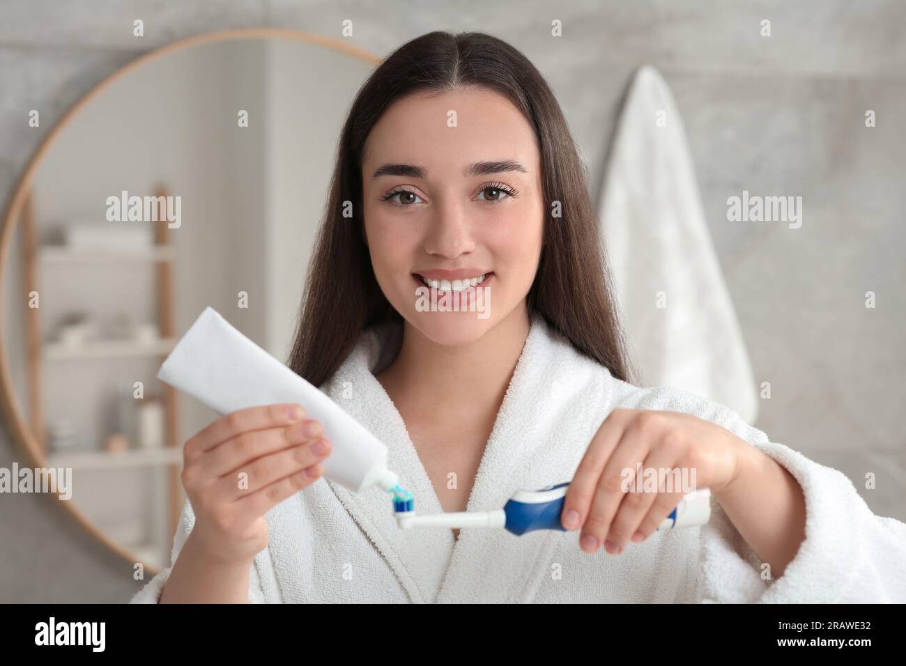 Young woman squeezing toothpaste from tube onto electric toothbrush in ...